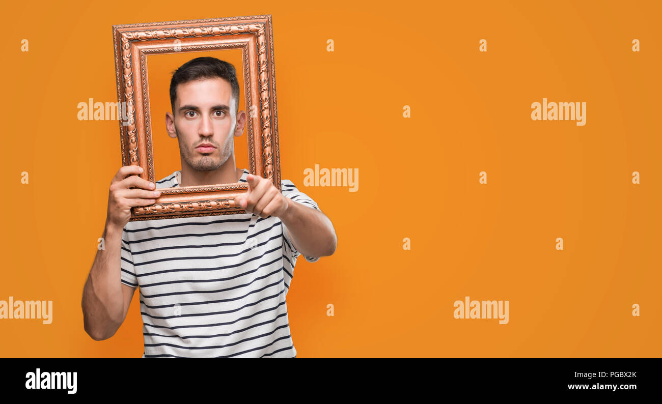 Handsome young man looking through vintage art frame pointing with ...