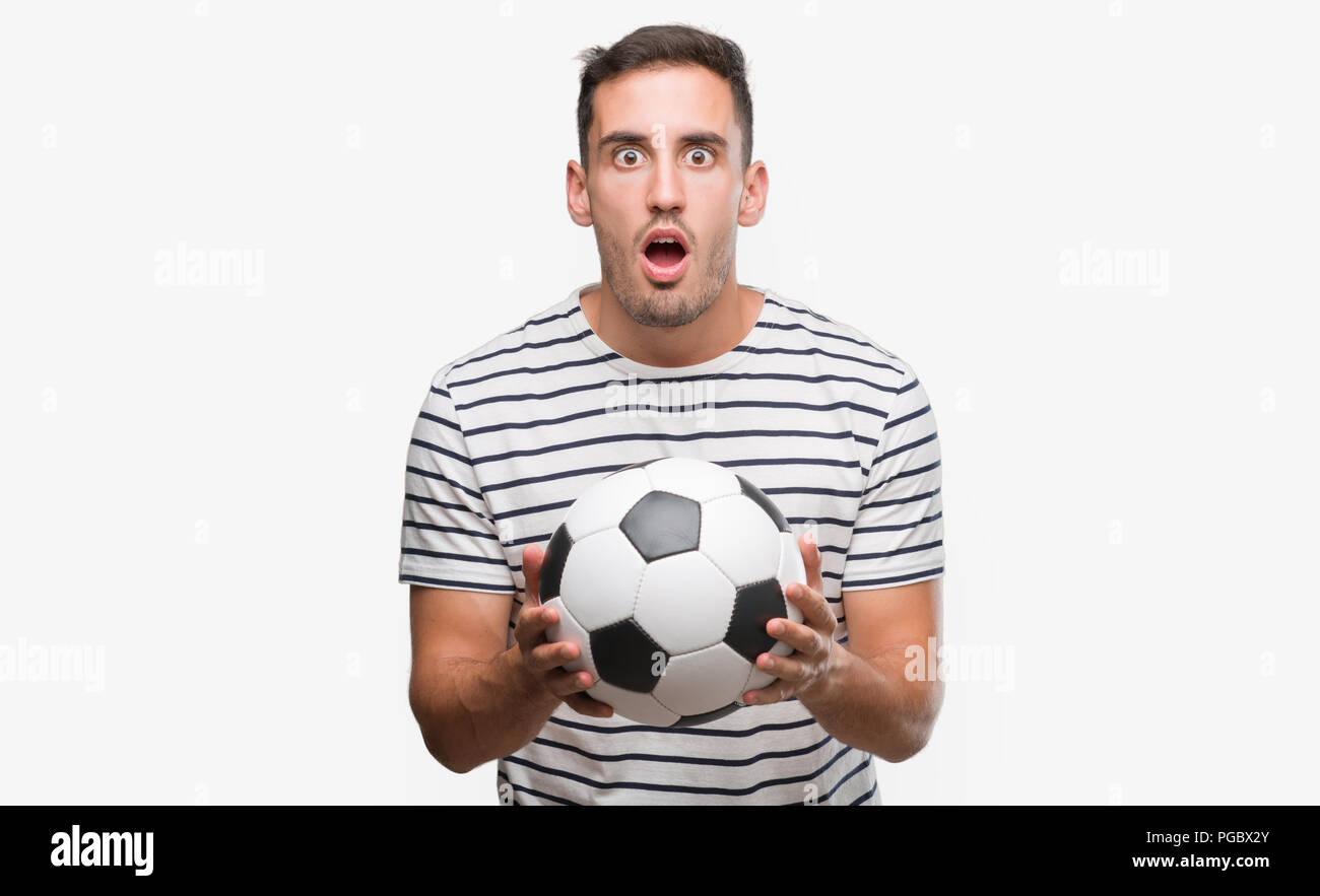 Handsome young man holding soccer football scared in shock with a ...