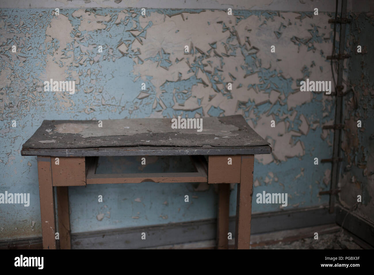 Aging table in front of the wall with peeled of blue paint in abandoned ...
