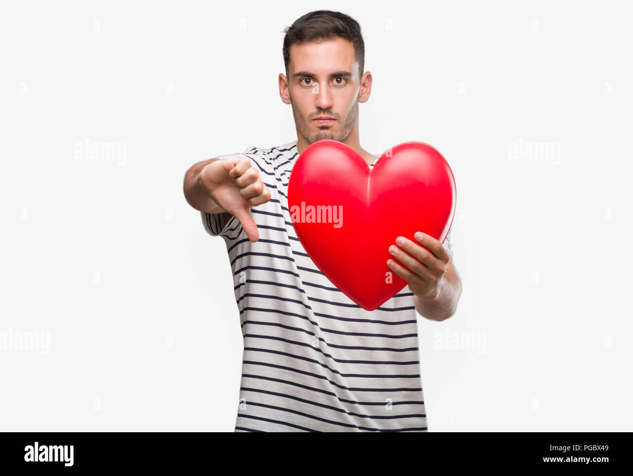 Handsome young man in love holding red heart with angry face, negative ...