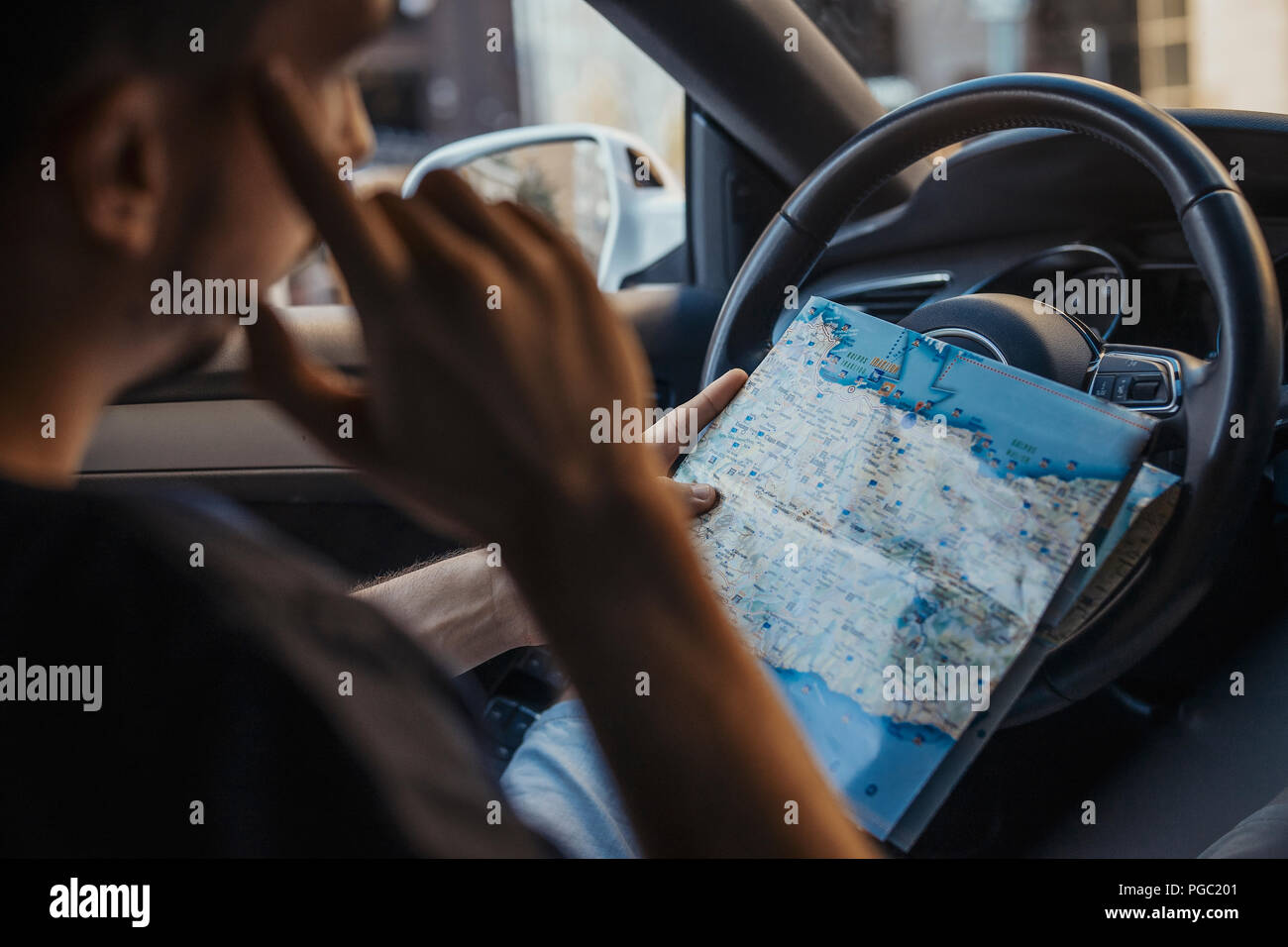 Close up of young man looking at map behind the wheel in car. Man is on ...