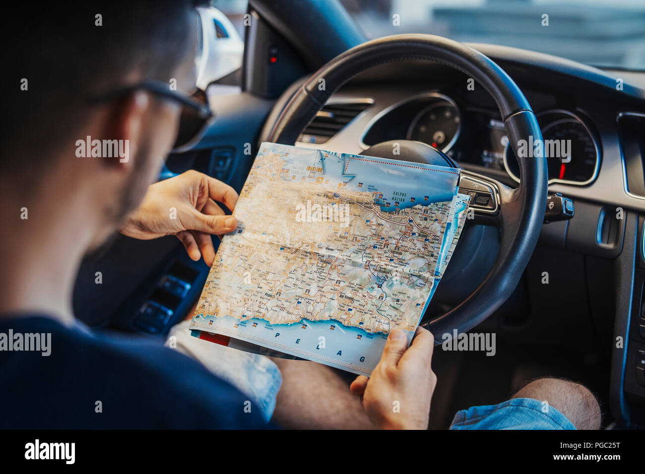 Close up of young man looking at map behind the wheel in car. Man is on ...