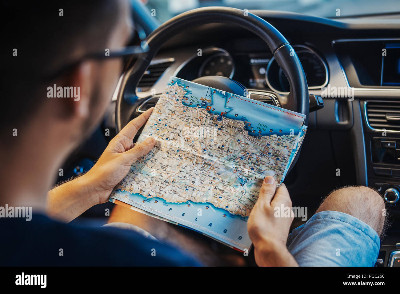Close up of young man looking at map behind the wheel in car. Man is on ...