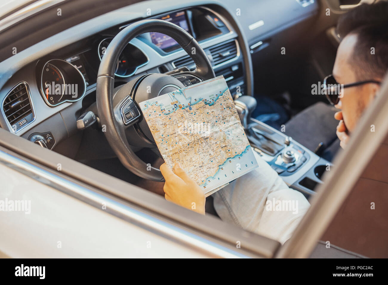 Close up of young man looking at map behind the wheel in car. Man is on ...