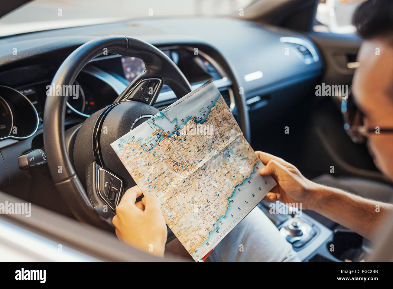 Close up of young man looking at map behind the wheel in car. Man is on ...