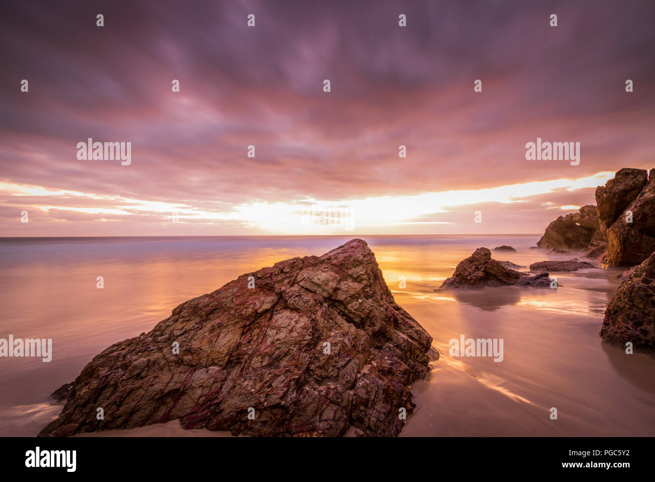 Cloudy sunrise over ocean and rocky beach Stock Photo - Alamy