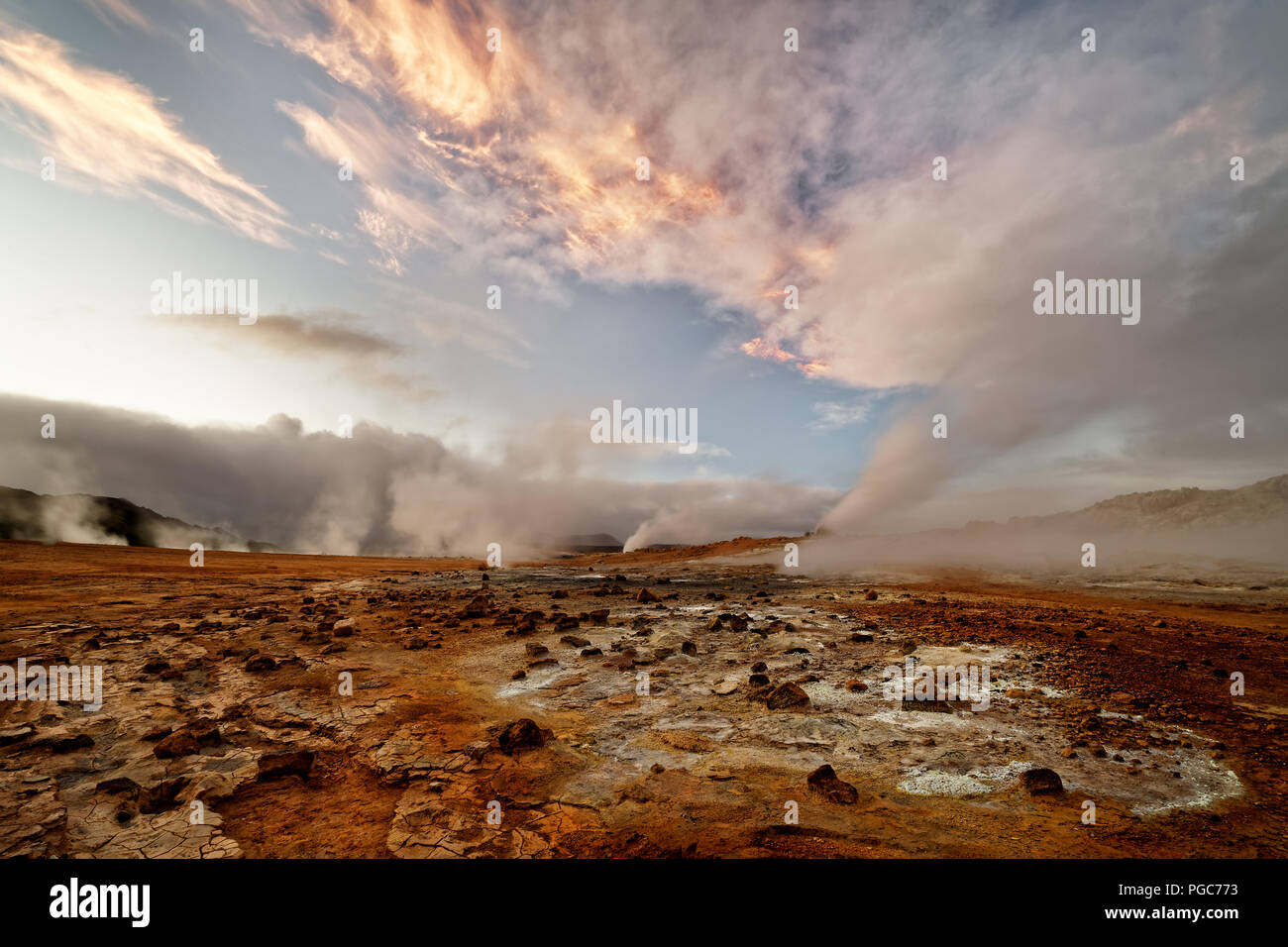 Wide view over a volcanic landscape with reddish ground, rising steam ...