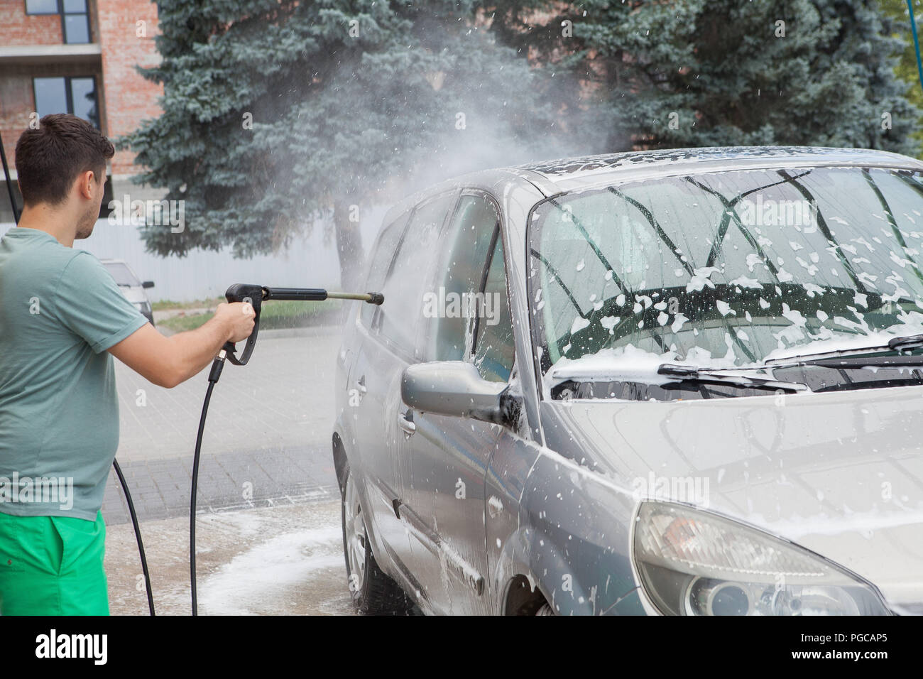 Caucasian man is spraying cleaning water to a modern car in car wash ...