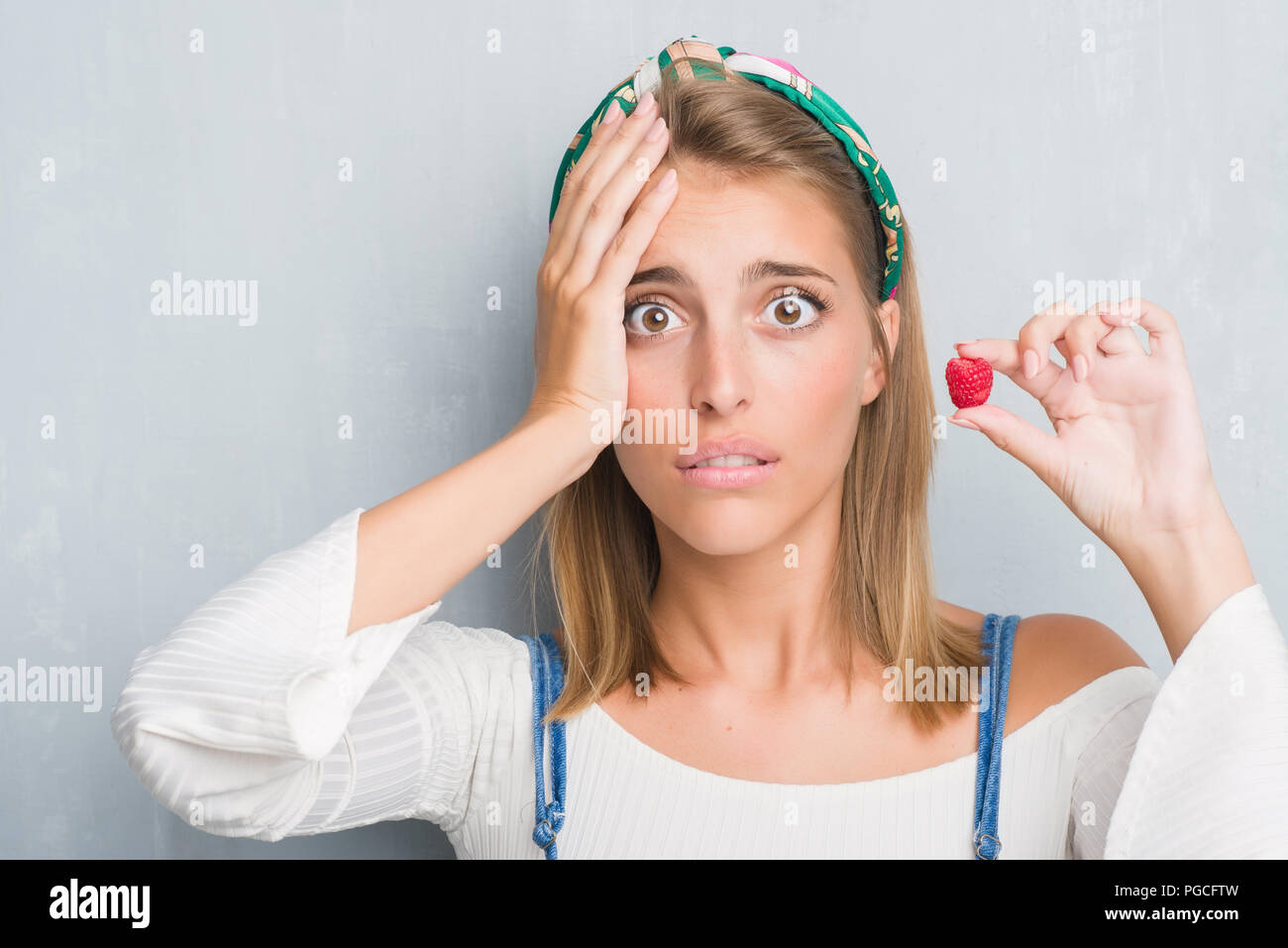 Beautiful young woman over grunge grey wall eating fresh raspberry ...