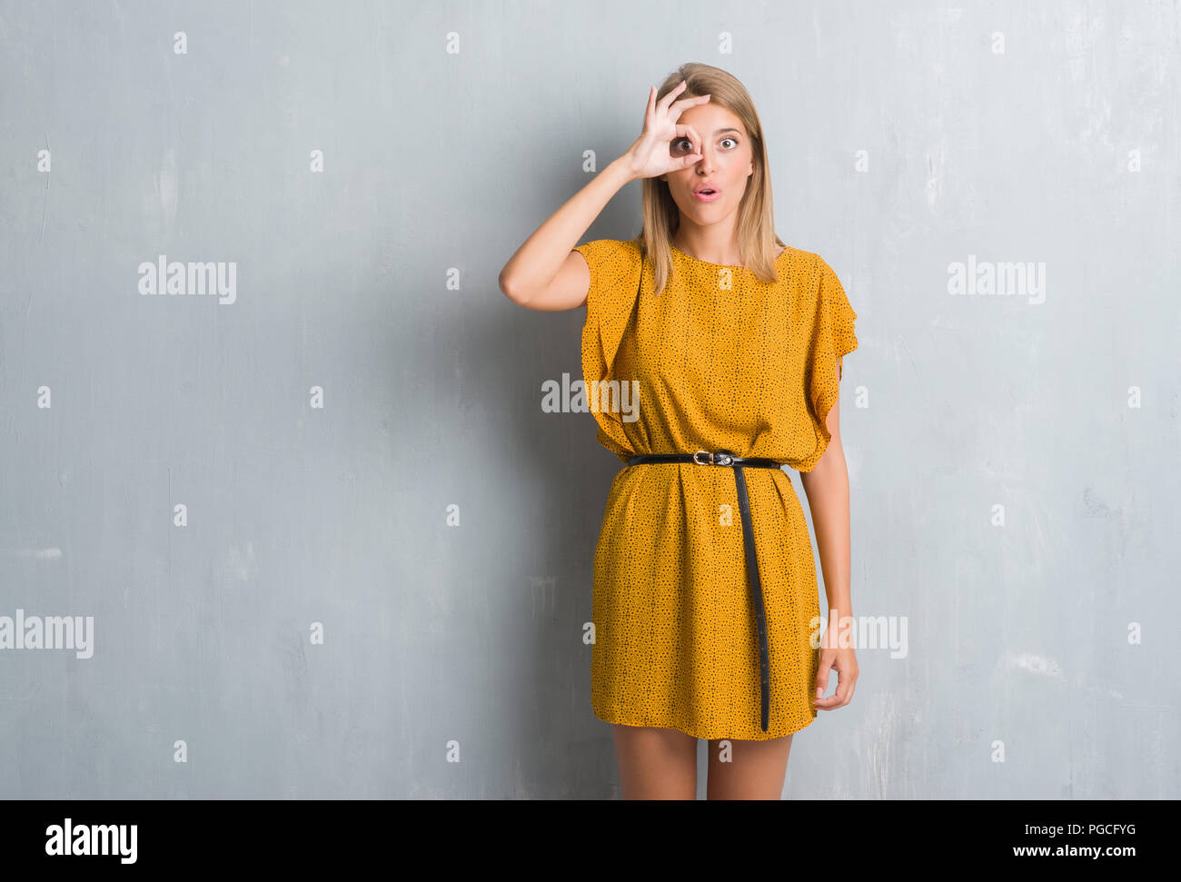 Beautiful young woman standing over grunge grey wall wearing a dress ...