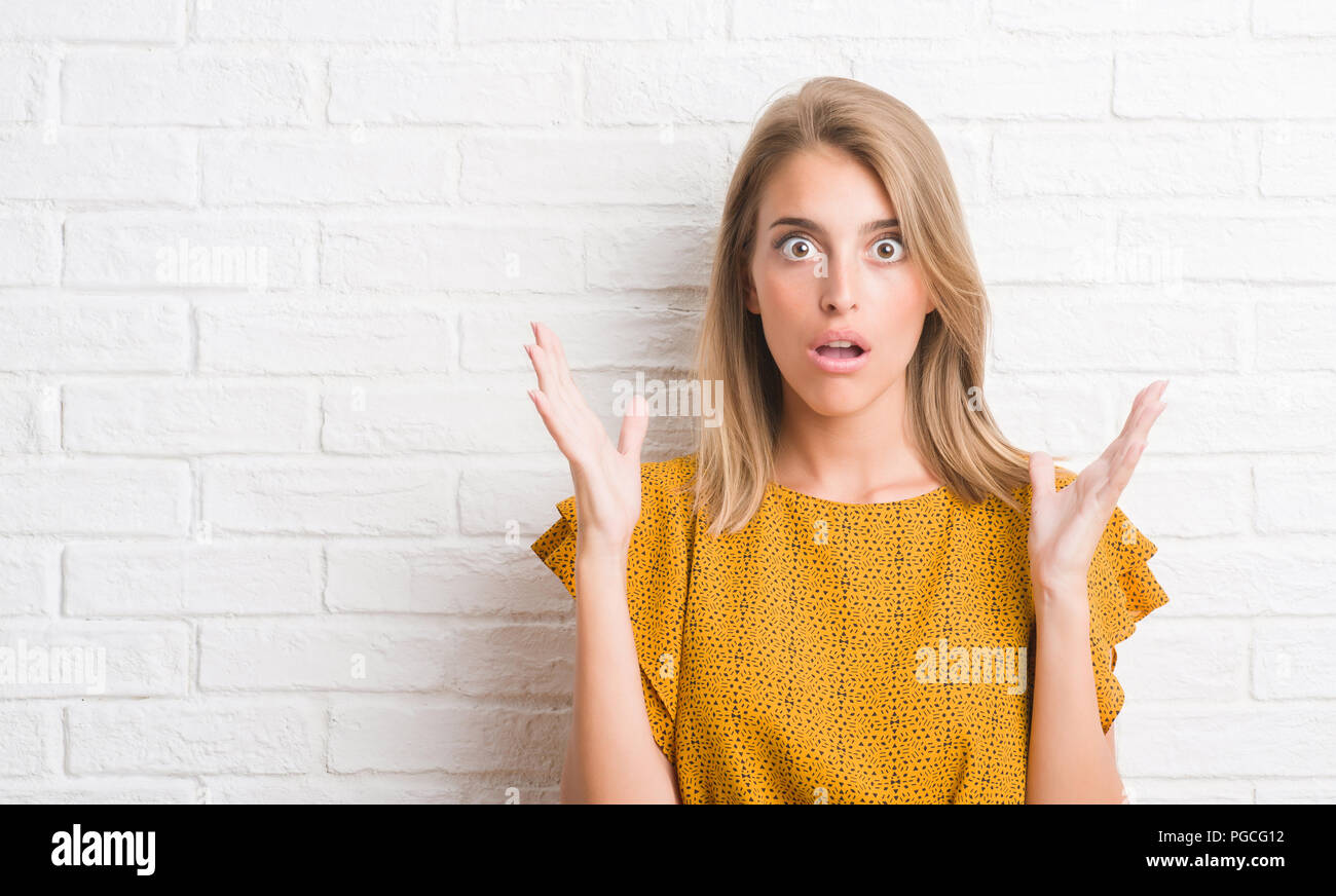 Beautiful young woman over white brick wall scared in shock with a ...
