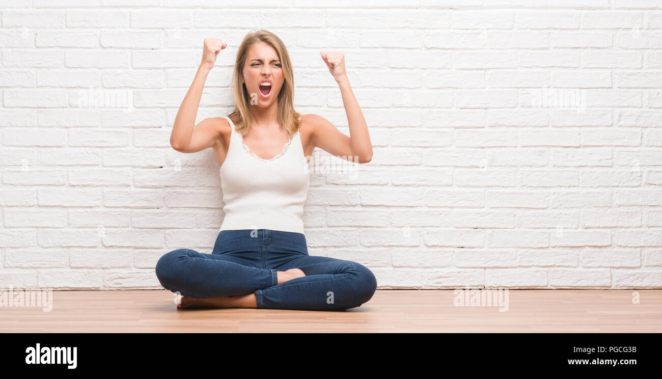 Beautiful young woman sitting on the floor at home angry and mad ...