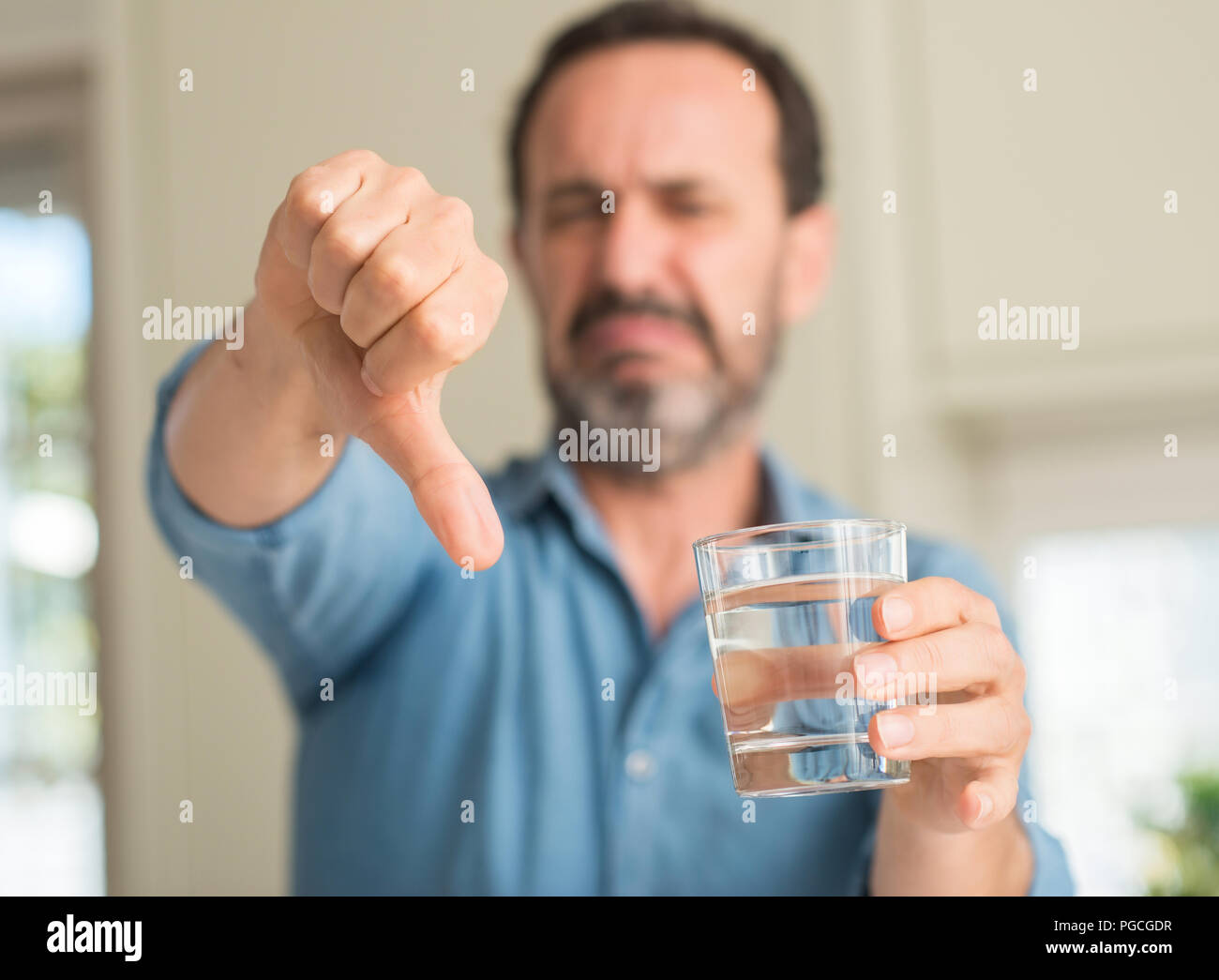 Middle age man drinking a glass of water with angry face, negative sign ...