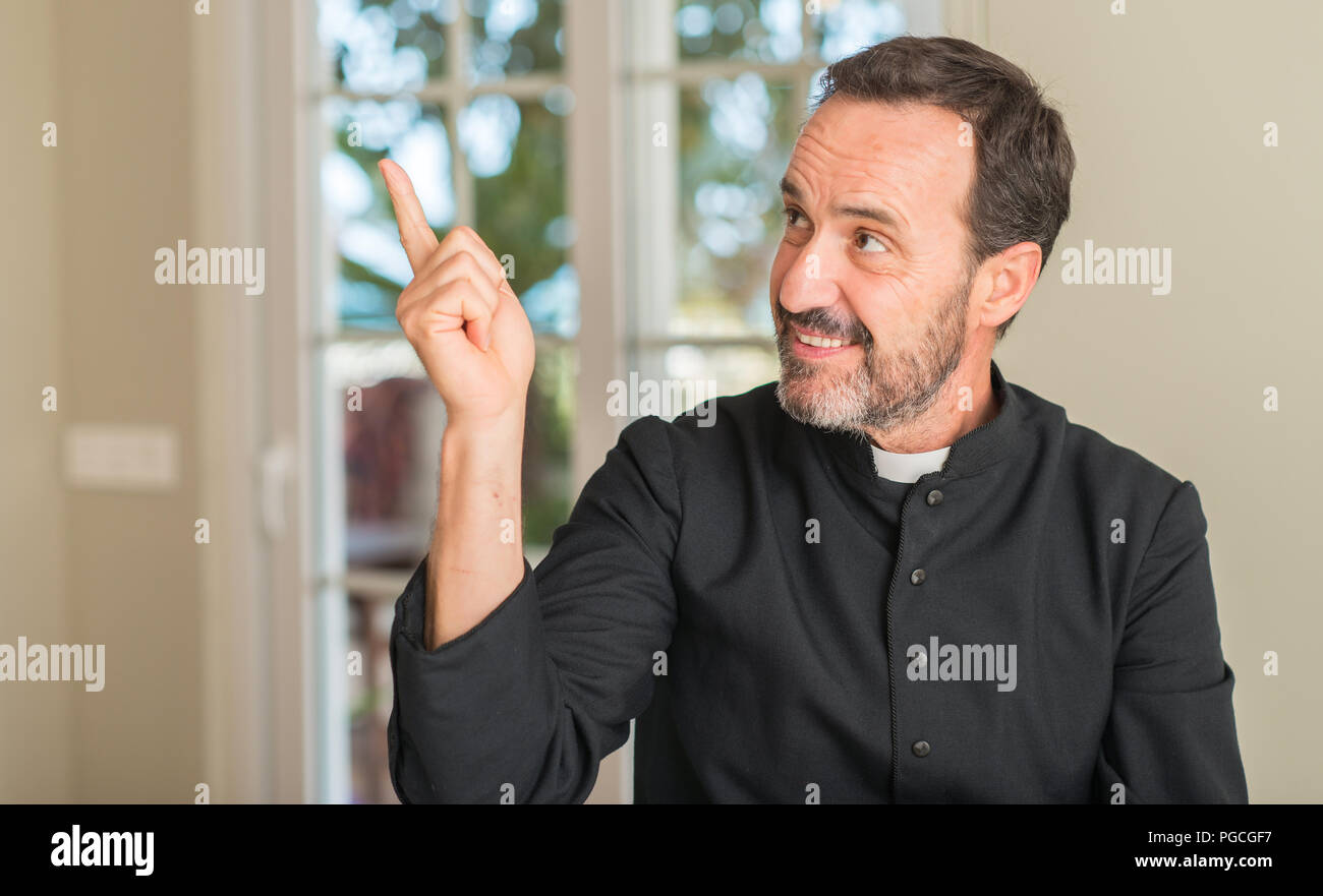 Christian priest man very happy pointing with hand and finger to the ...