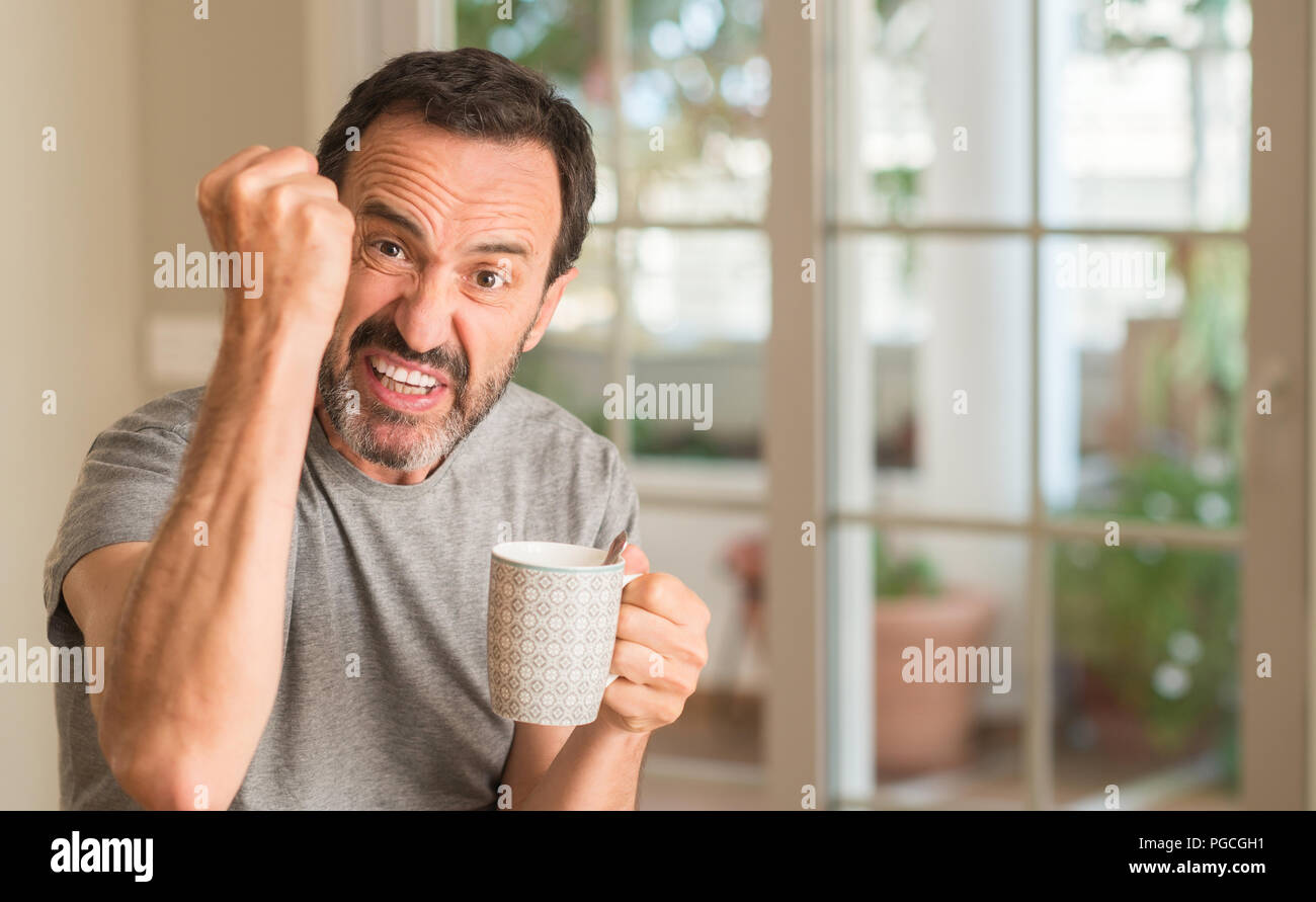 Middle age man drinking coffee in a cup annoyed and frustrated shouting ...