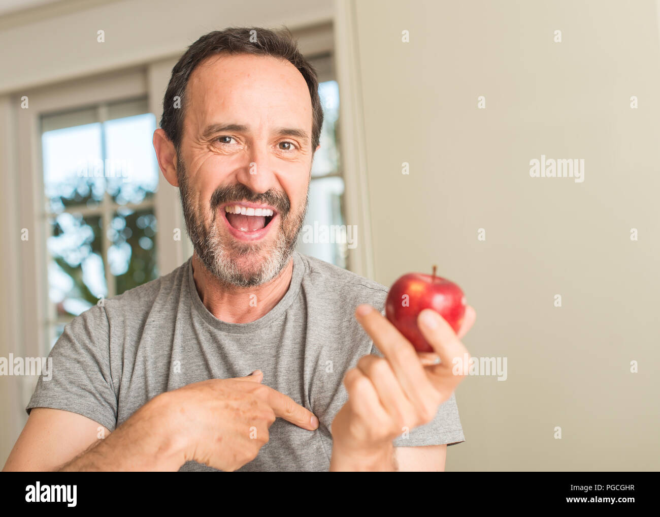 Middle age man eating healthy red apple with surprise face pointing ...