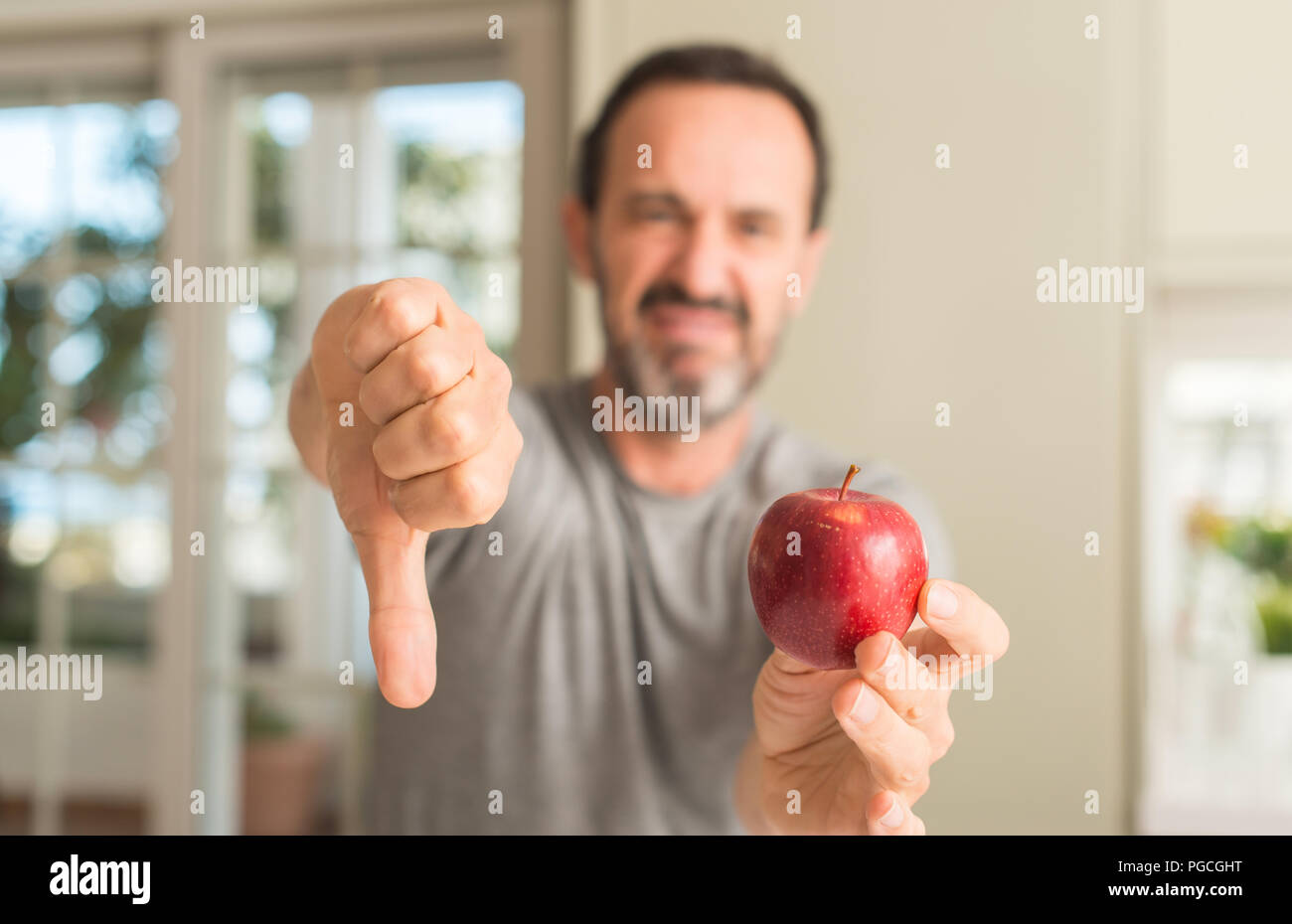 Middle age man eating healthy red apple with angry face, negative sign ...