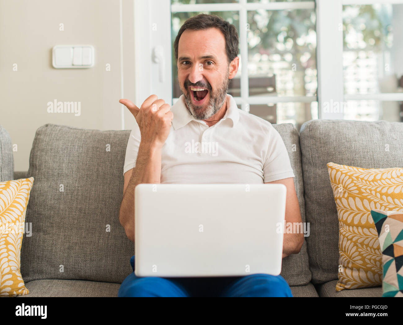 Middle age man using laptop at sofa pointing with hand and finger up ...
