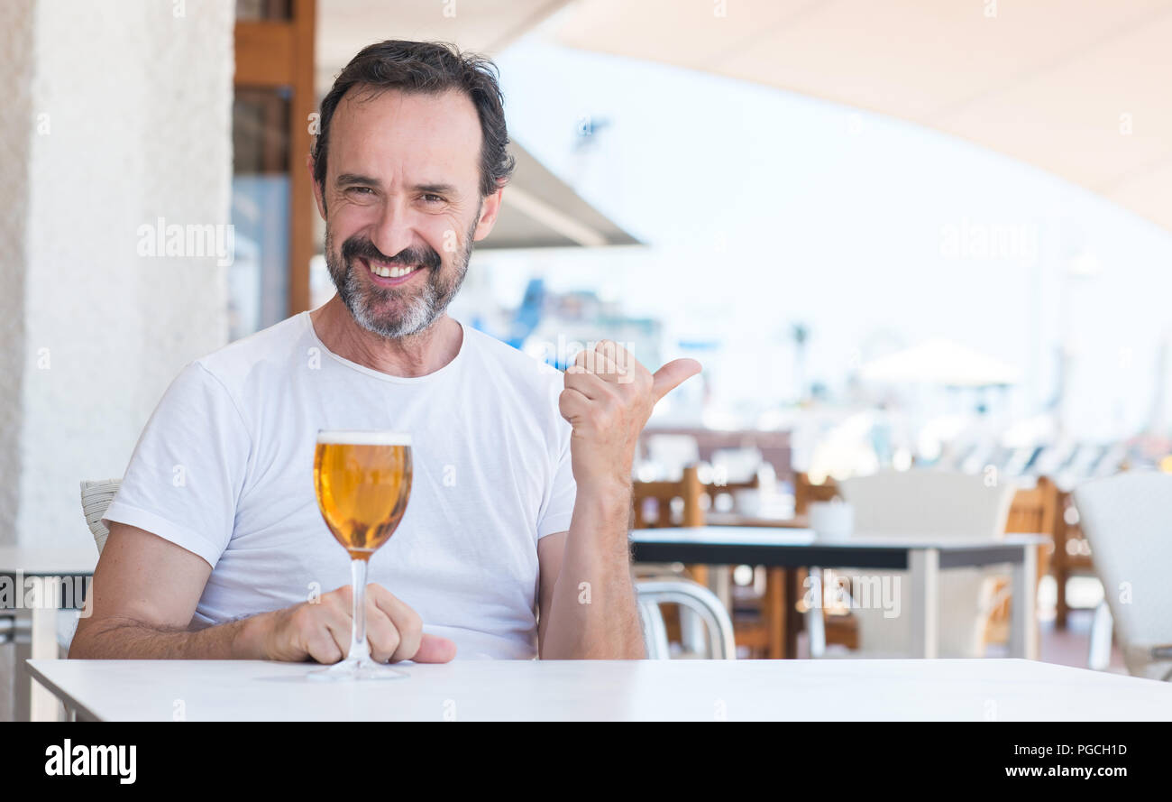 Handsome senior man drinking beer at restaurant pointing with hand and ...