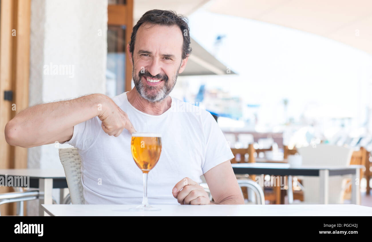 Handsome senior man drinking beer at restaurant with surprise face ...