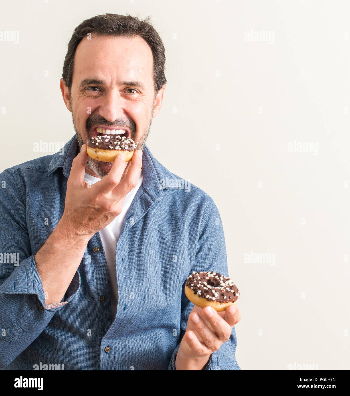 Senior man eating chocolate donut with a happy face standing and ...