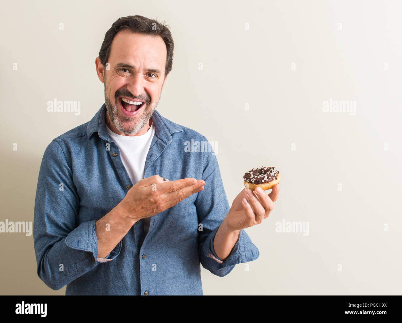 Senior man eating chocolate donut very happy pointing with hand and ...