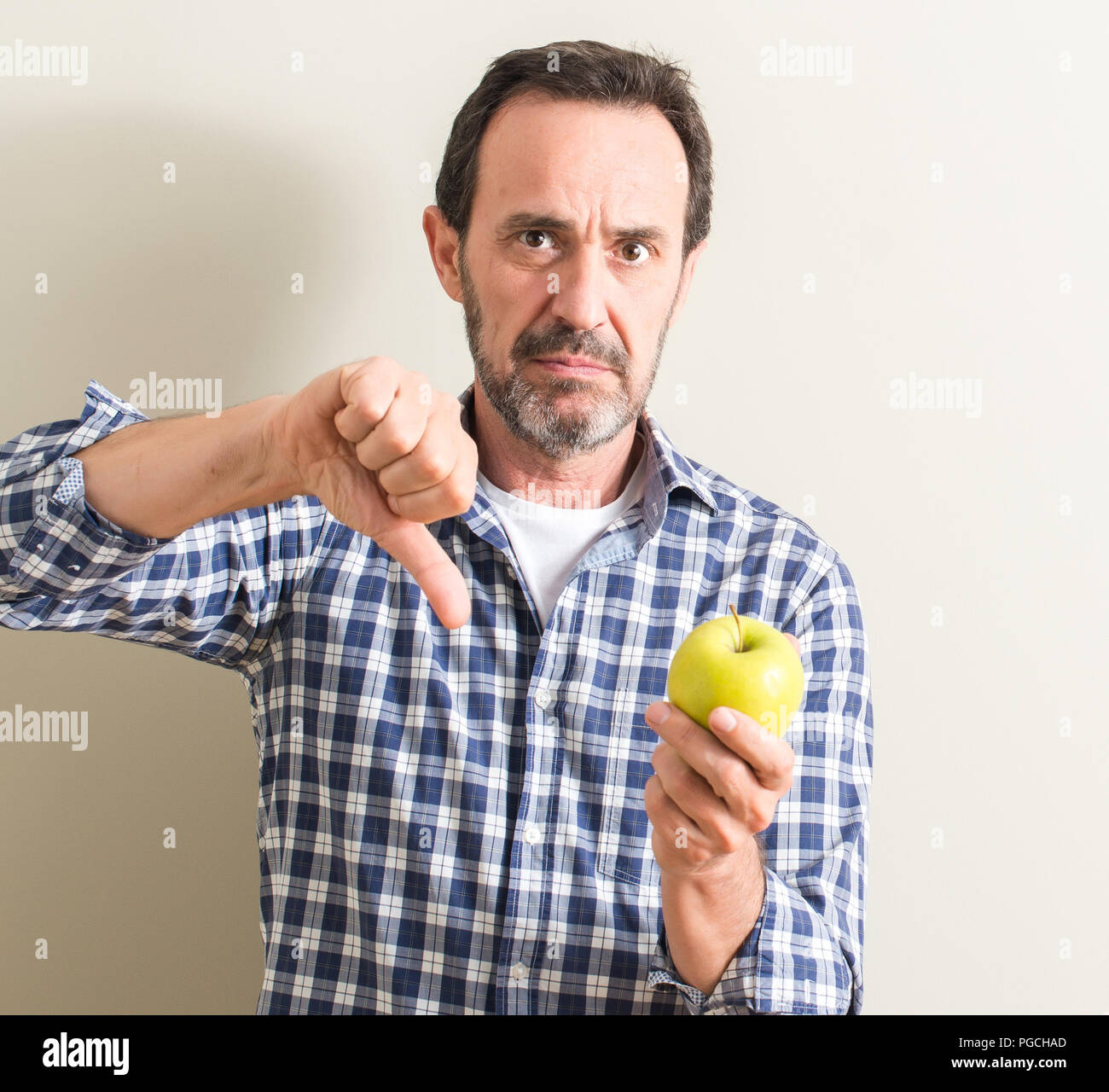 Senior man holding a green apple with angry face, negative sign showing ...