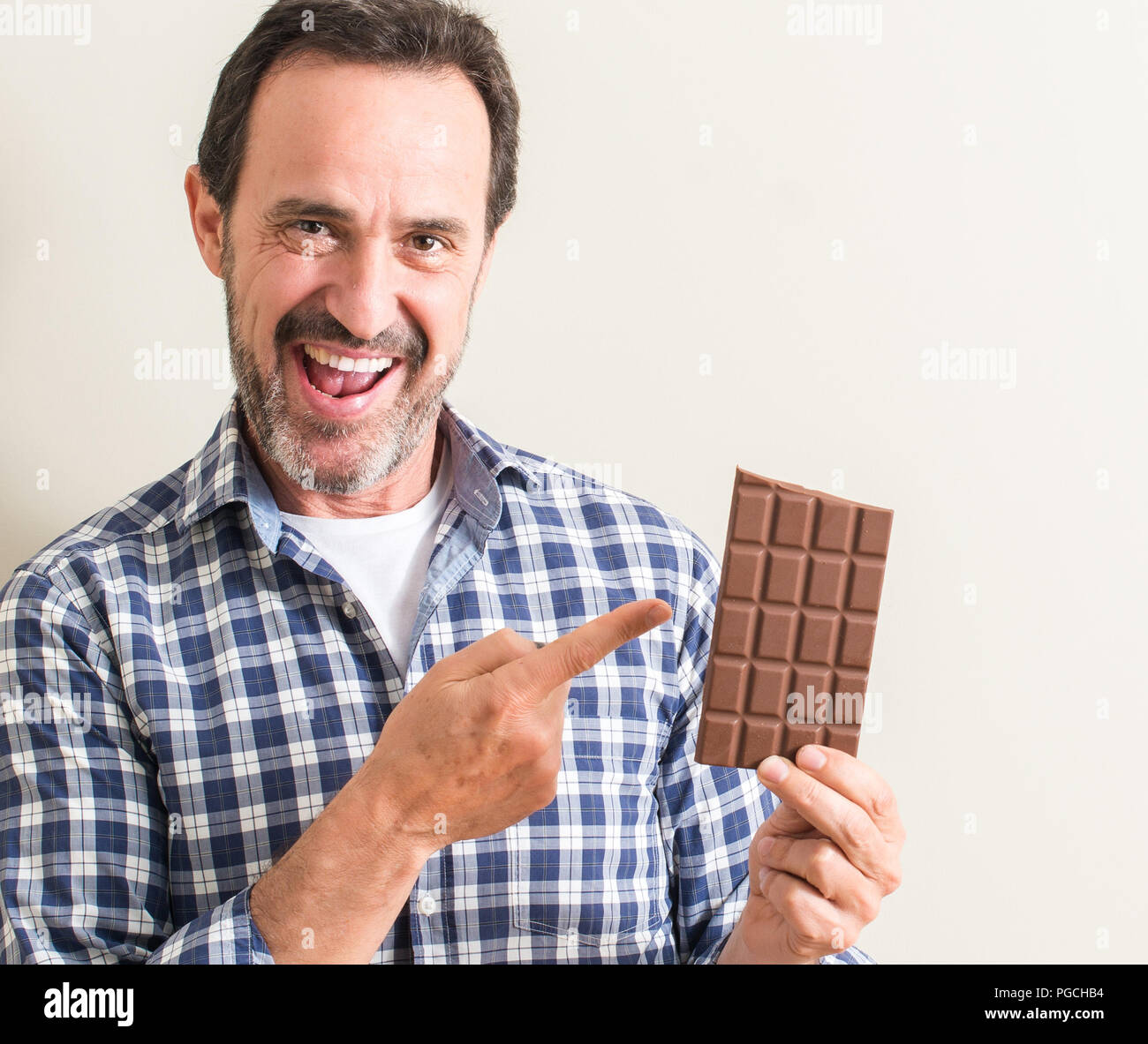 Senior man eating chocolate bar very happy pointing with hand and ...