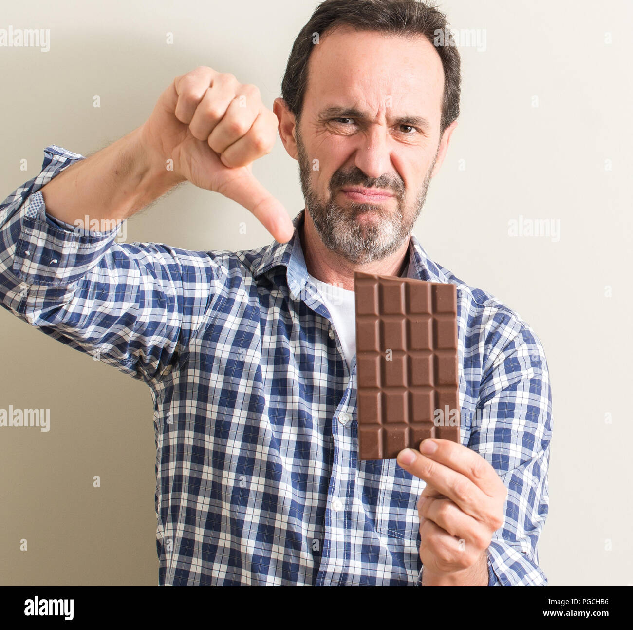 Senior man eating chocolate bar with angry face, negative sign showing ...