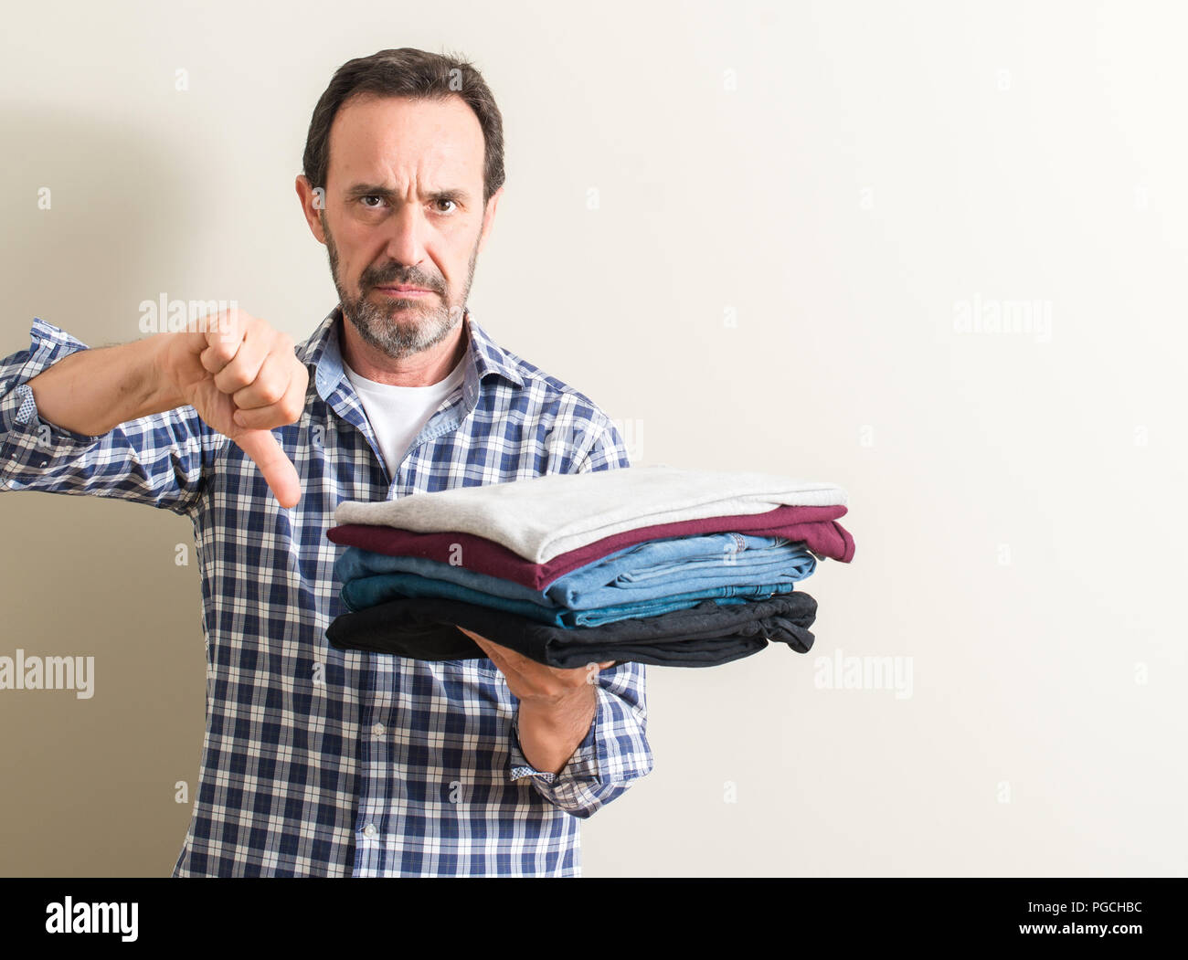 Senior man holding folded laundry clothes with angry face, negative ...