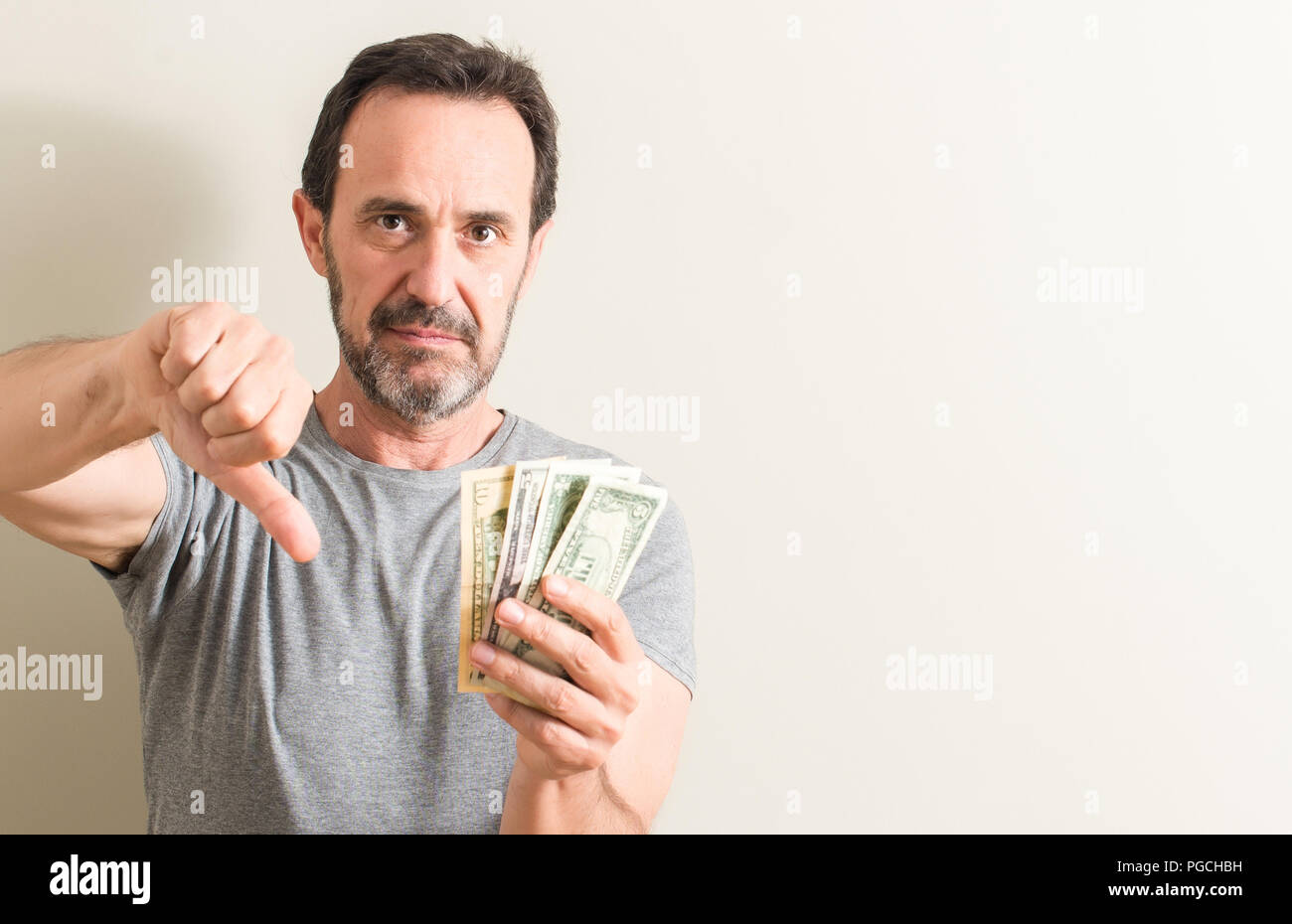 Senior man holding dollar money with angry face, negative sign showing ...