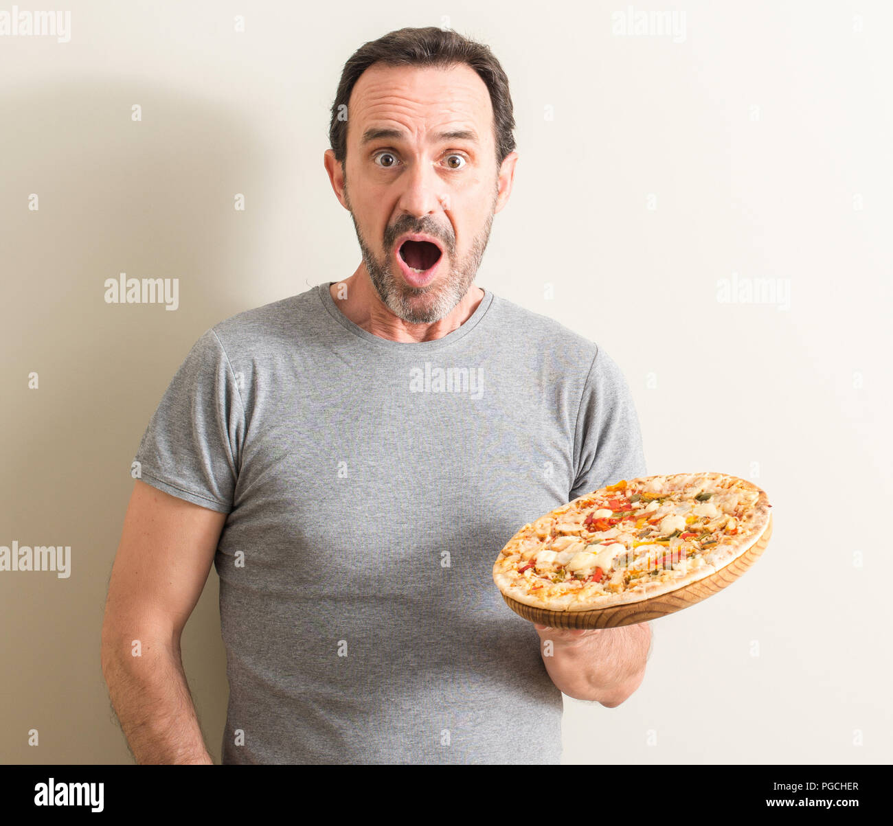 Senior man holding pizza scared in shock with a surprise face, afraid ...