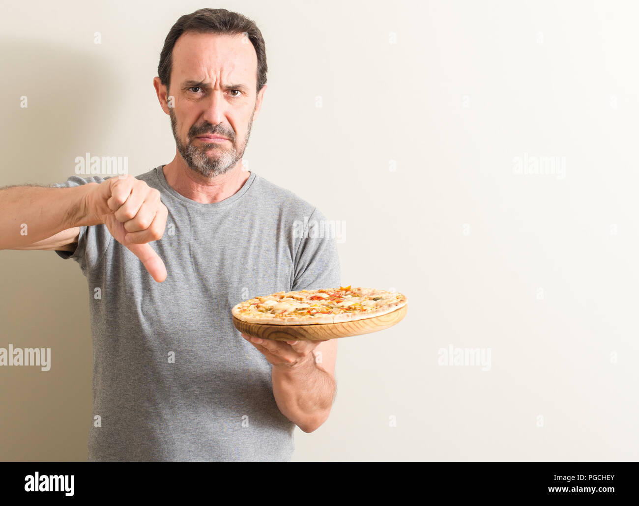 Senior man holding pizza with angry face, negative sign showing dislike ...