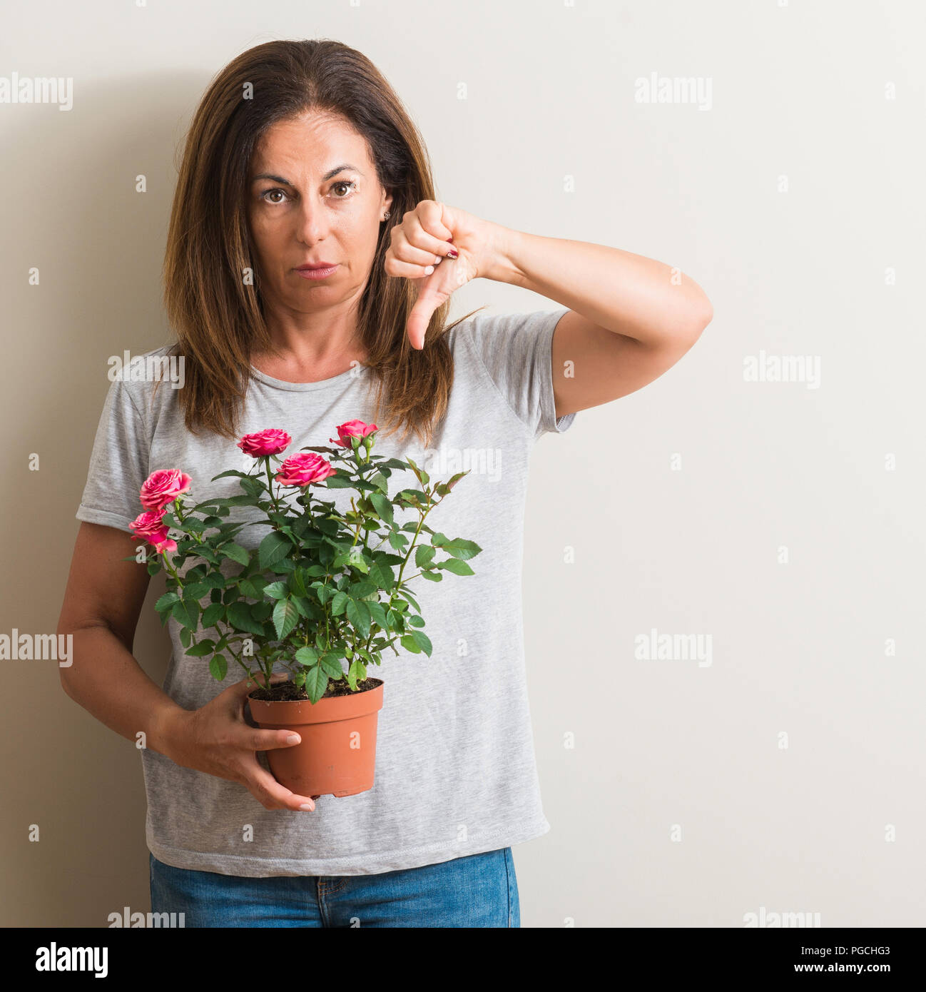 Middle age woman holding roses flowers on pot with angry face, negative ...