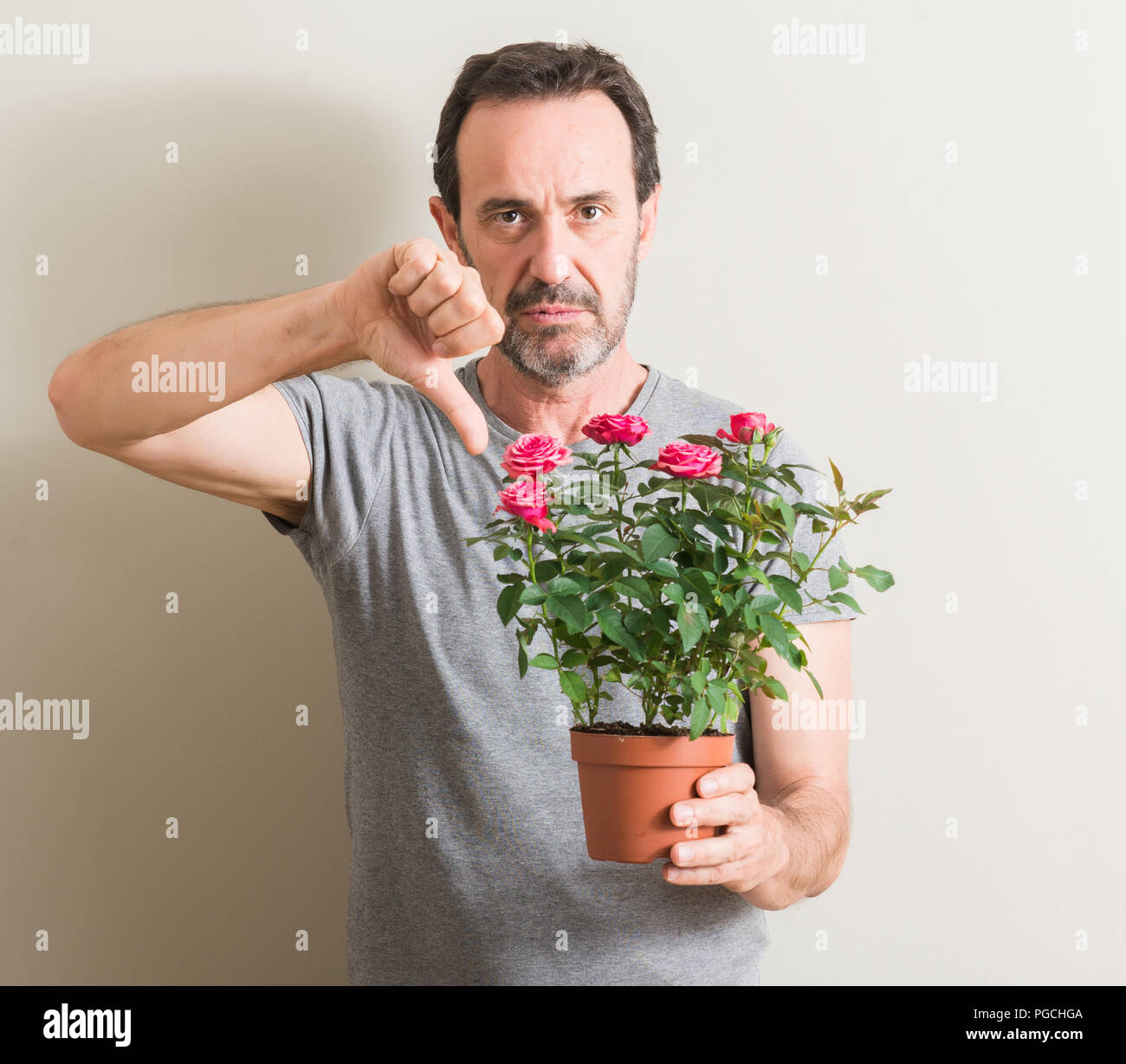 Senior man holding roses flowers on pot with angry face, negative sign ...