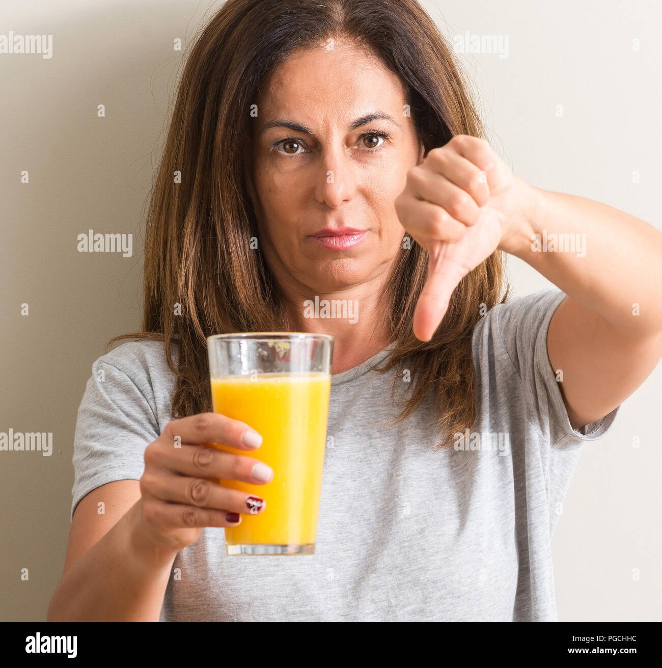 Middle age woman drinking orange juice in a glass with angry face ...