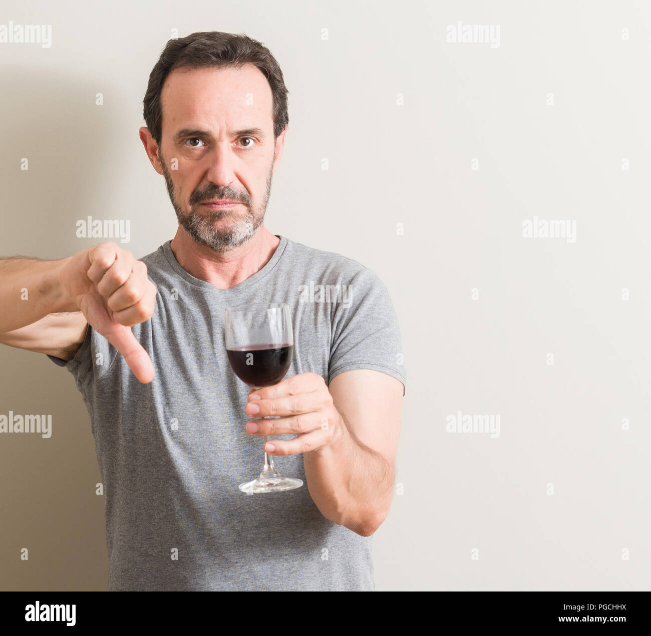 Senior man drinking red wine in a glass with angry face, negative sign ...