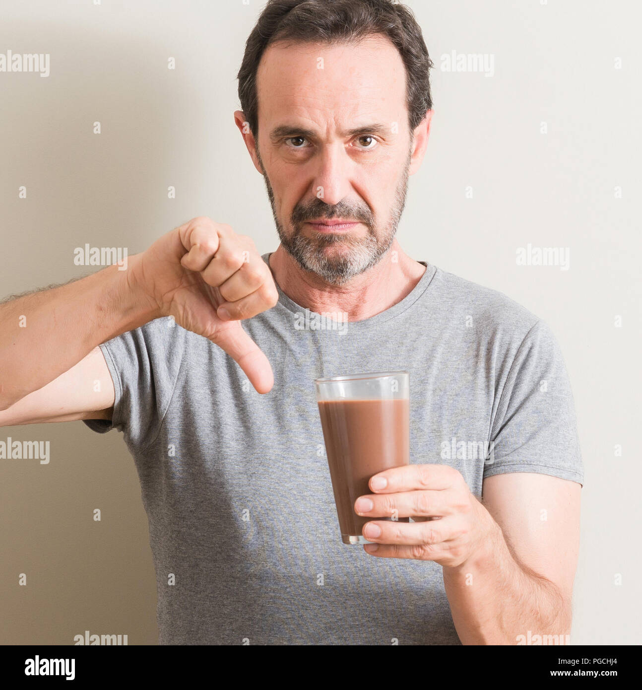 Senior man drinking chocolate milk shake with angry face, negative sign ...