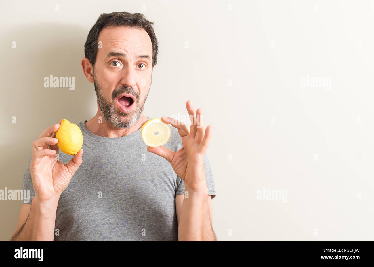 Senior man holding lemon fruit scared in shock with a surprise face ...