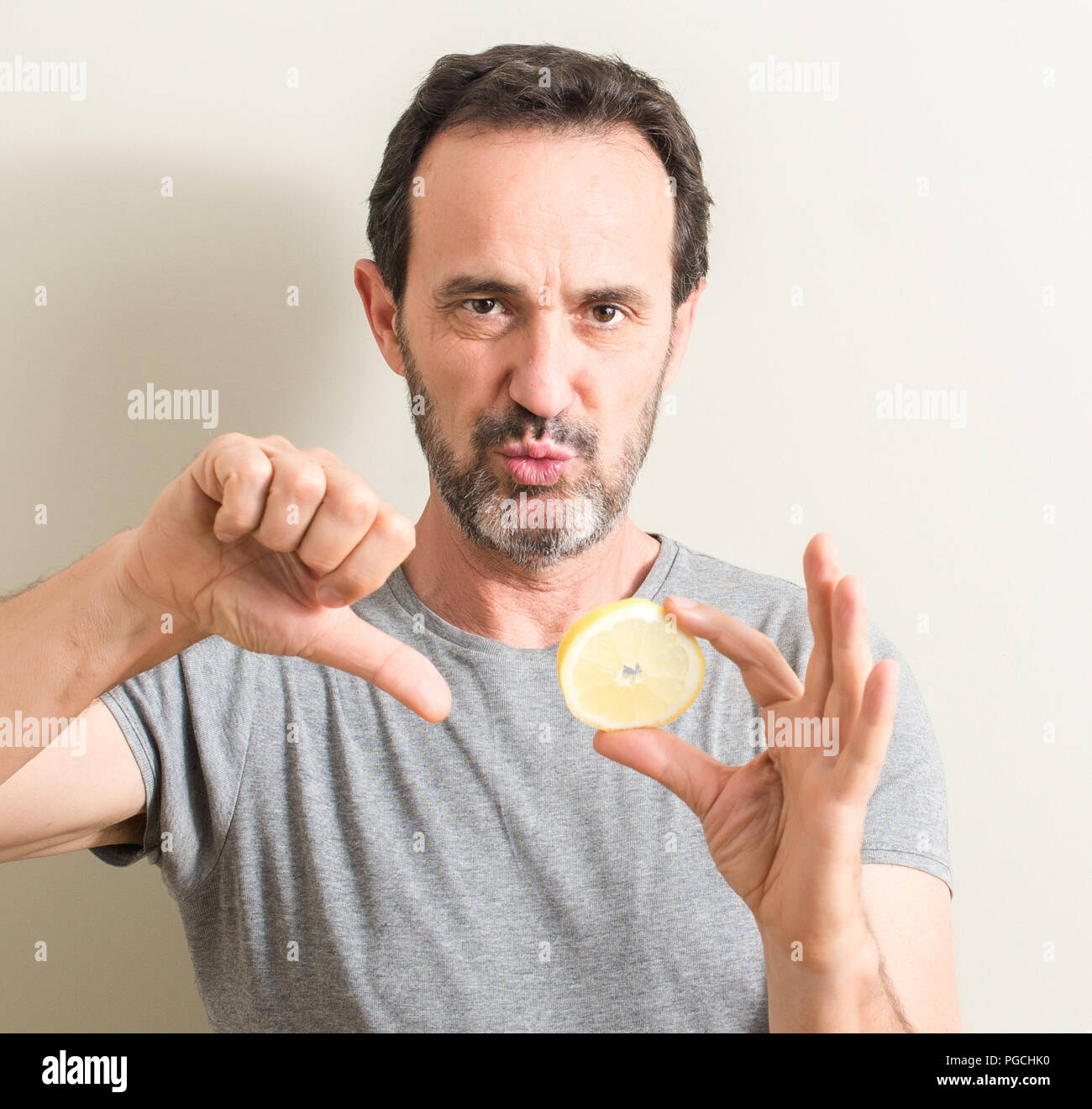 Senior man holding lemon fruit with angry face, negative sign showing ...