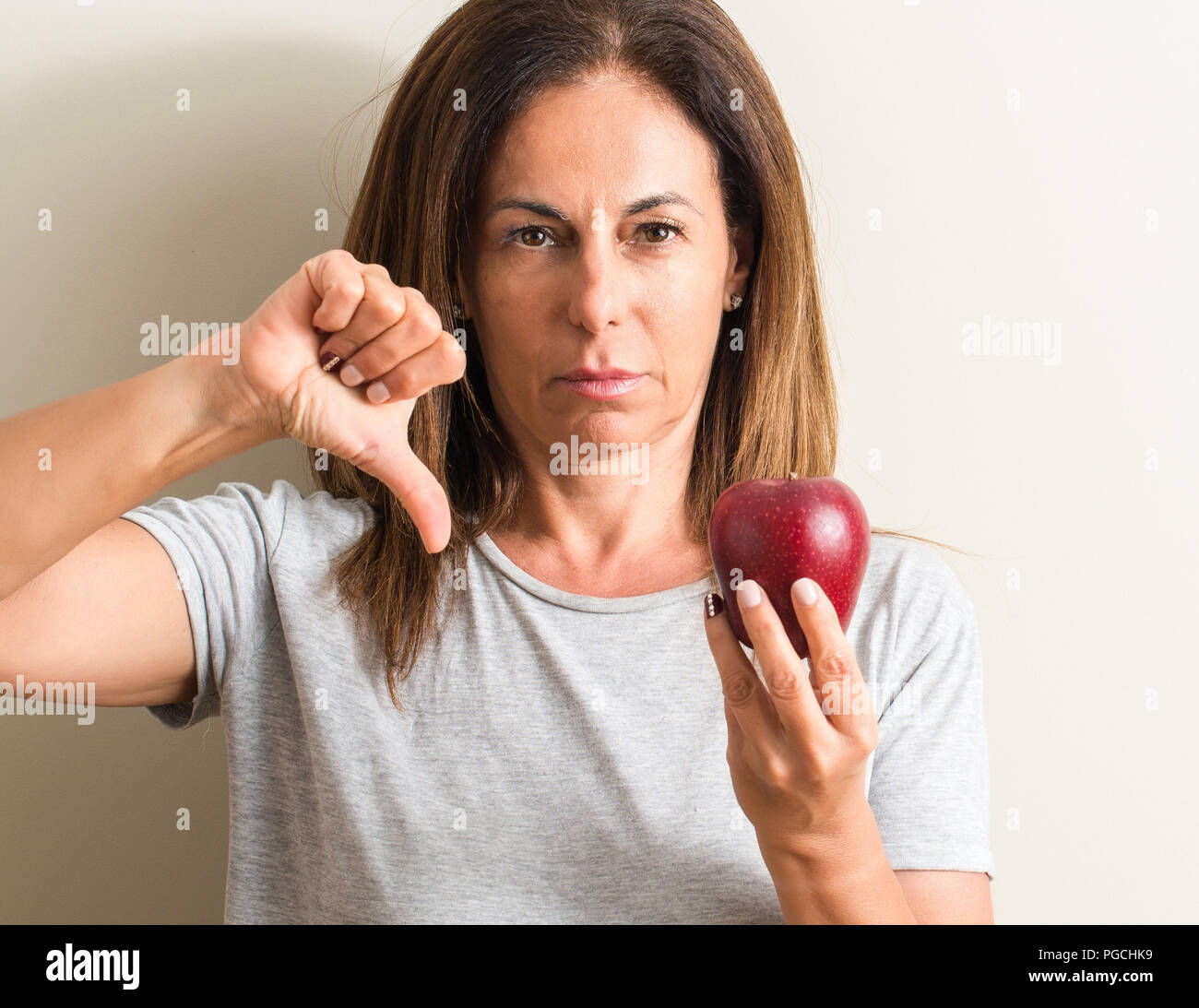 Middle age woman holding a green apple with angry face, negative sign ...