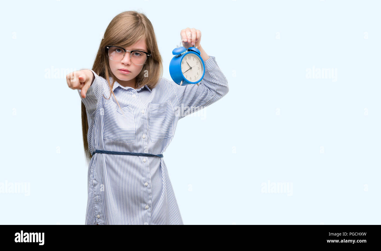 Young blonde child holding alarm clock pointing with finger to the ...