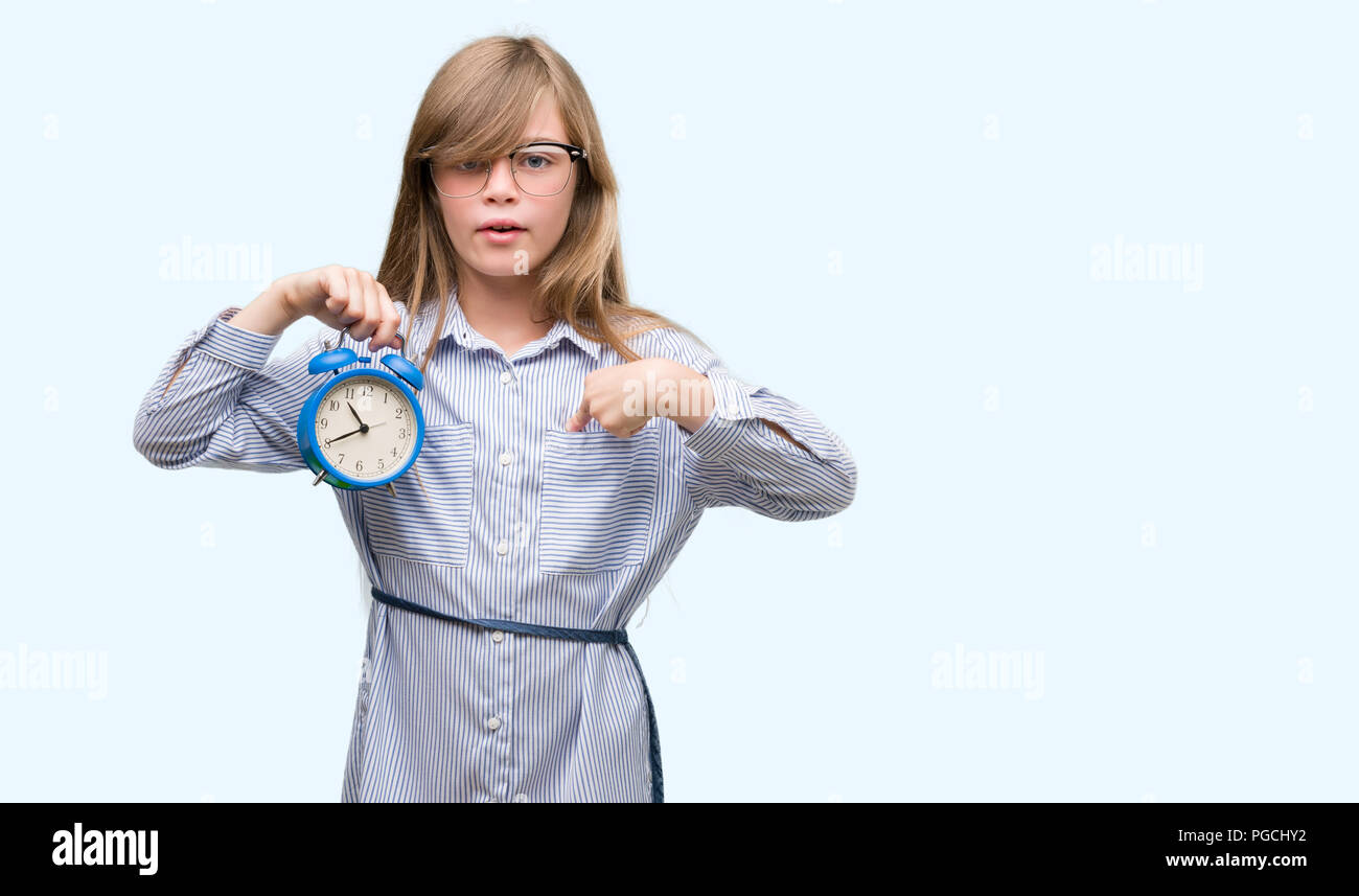 Young blonde child holding alarm clock with surprise face pointing ...
