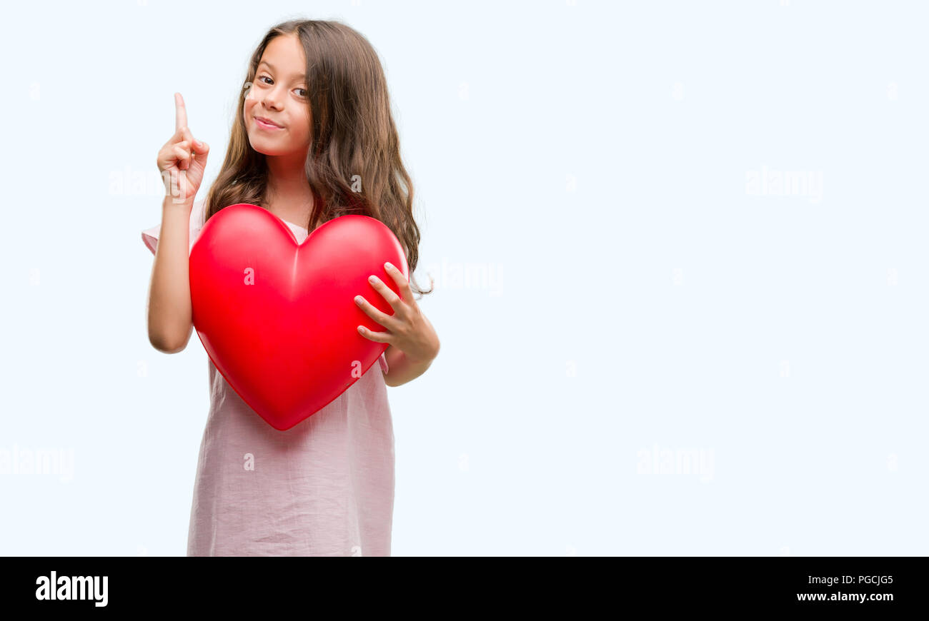 Brunette hispanic girl holding red heart surprised with an idea or ...