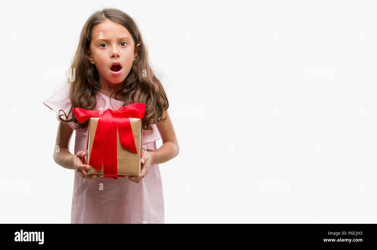 Brunette hispanic girl holding a gift scared in shock with a surprise ...