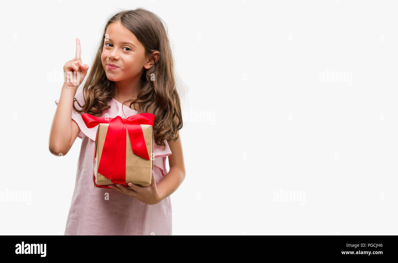 Brunette hispanic girl holding a gift surprised with an idea or ...