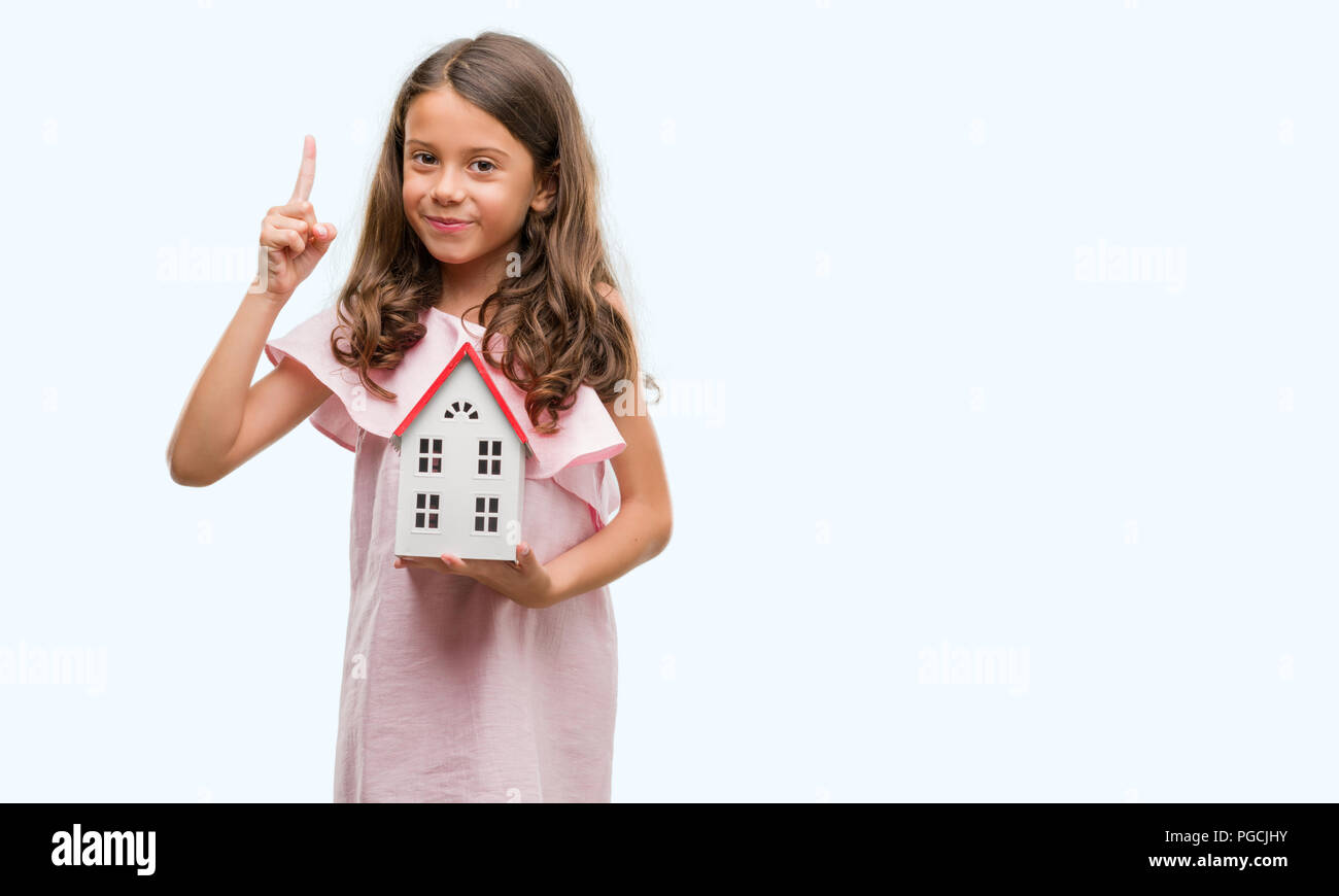 Brunette hispanic girl holding little house surprised with an idea or ...
