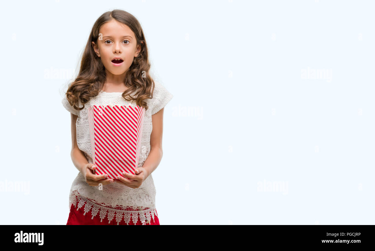 Brunette hispanic girl eating popcorn scared in shock with a surprise ...