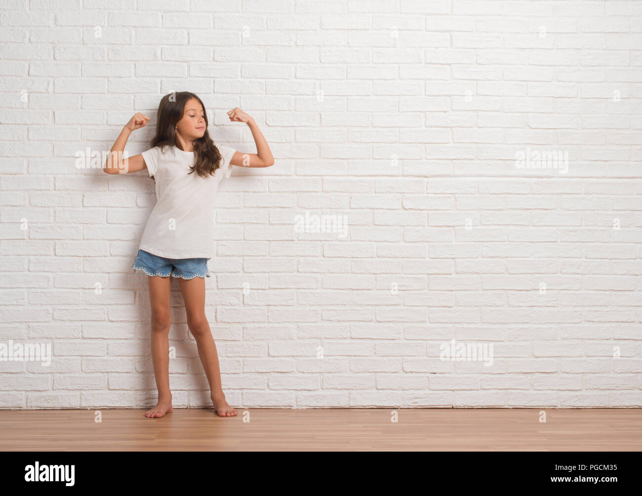 Young hispanic kid stading over white brick wall showing arms muscles ...