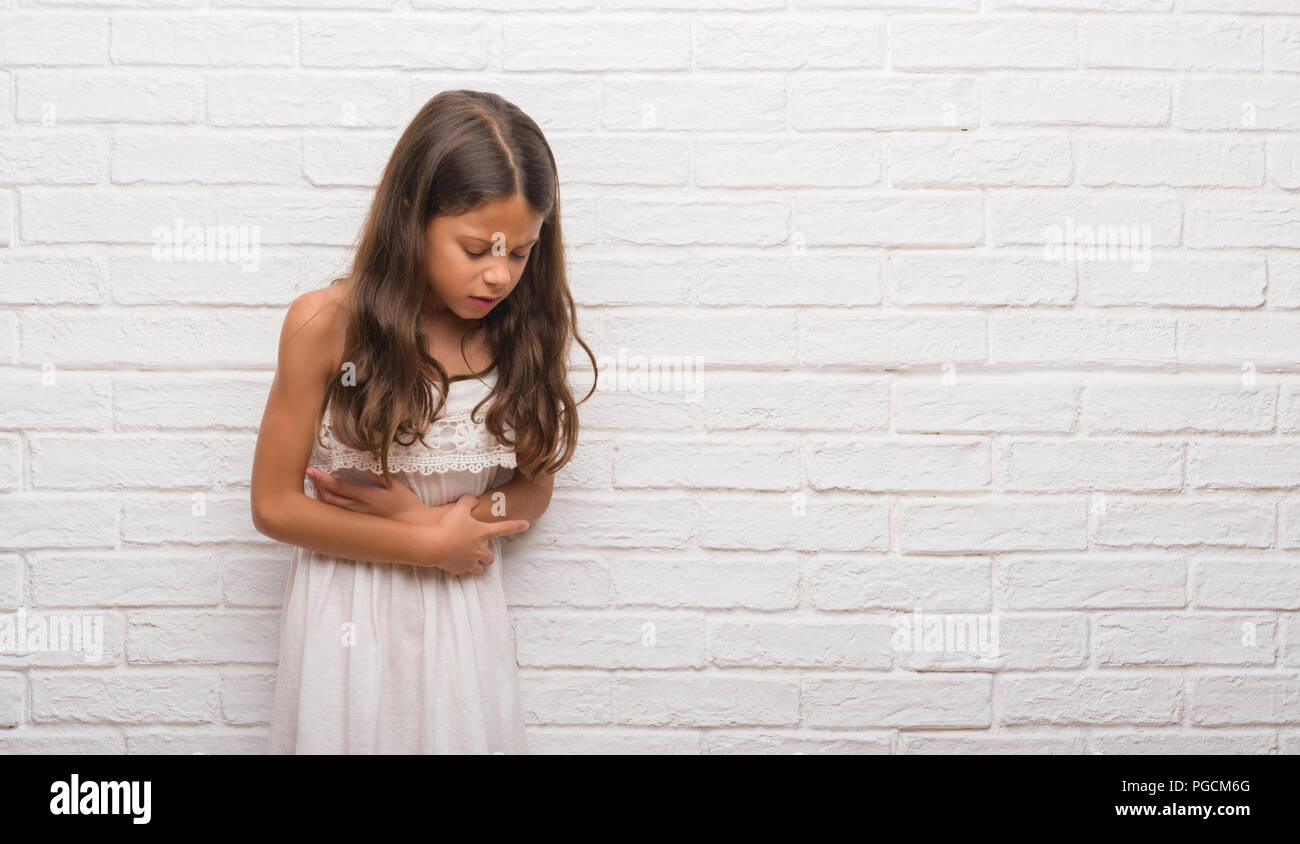 Young hispanic kid over white brick wall with hand on stomach because ...